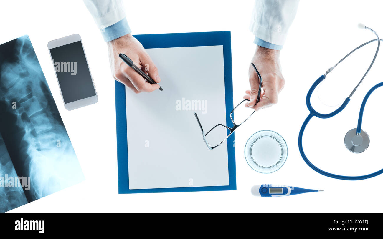 Doctor at desk with x ray and medical equipment writing a prescription ...