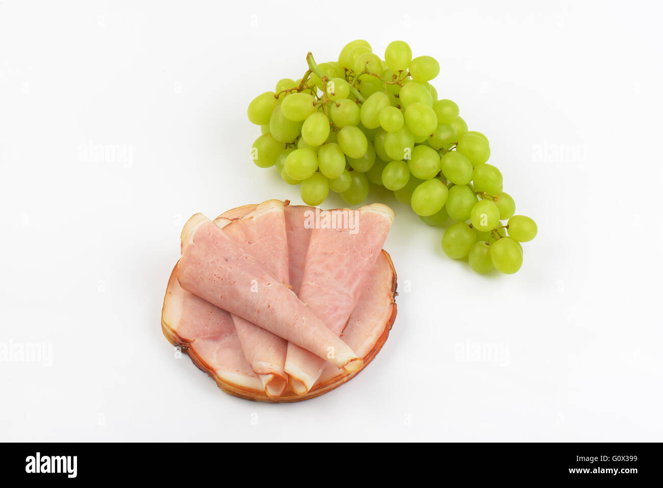 stack of ham slices and bunch of white grapes on white background Stock ...