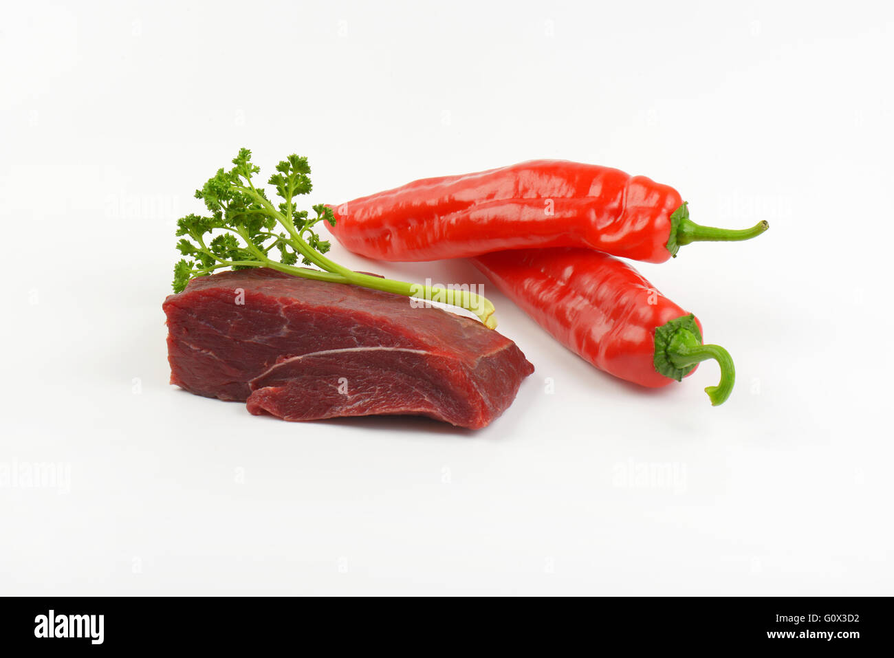 chunk of raw beef meat, fresh parsley and red pepper on white ...