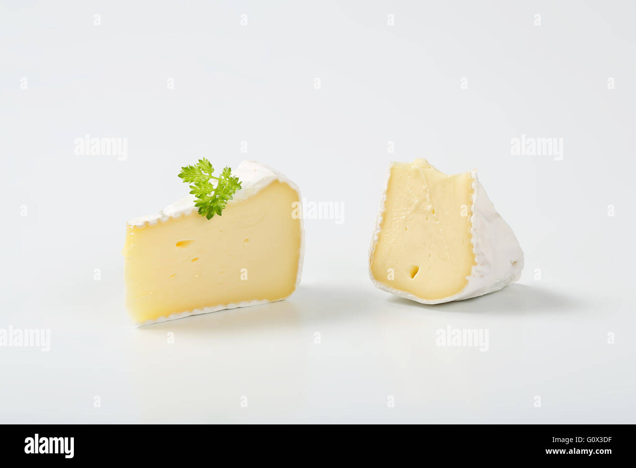 two slices of white rind cheese with parsley on white background Stock ...