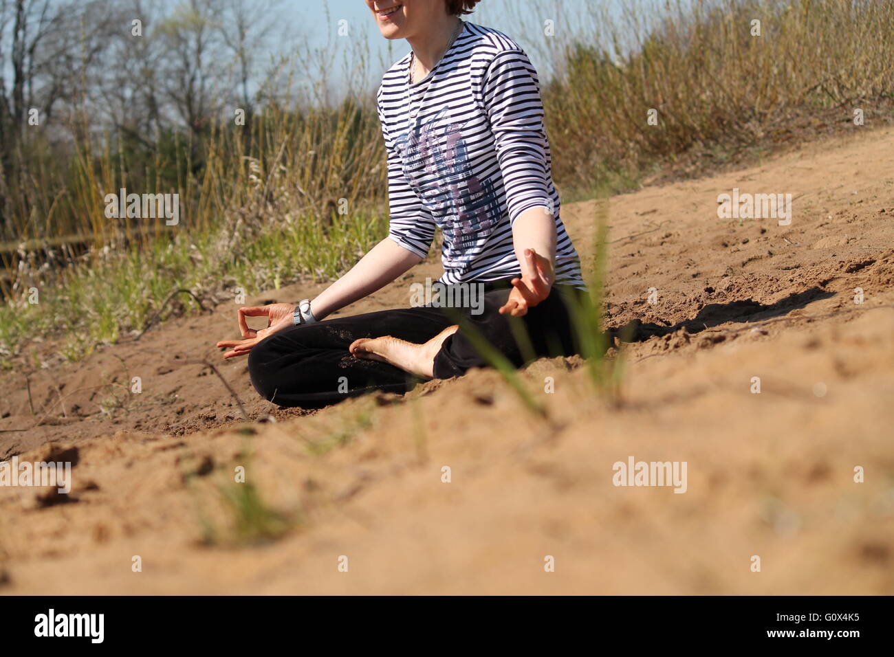 young woman sit in meditative pose lotus Padmasana on sunny sand land ...