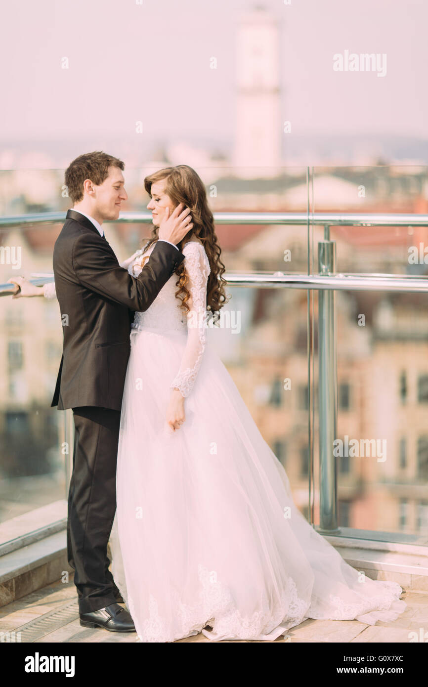Handsome groom gently touches face of his bride on the terrace ...