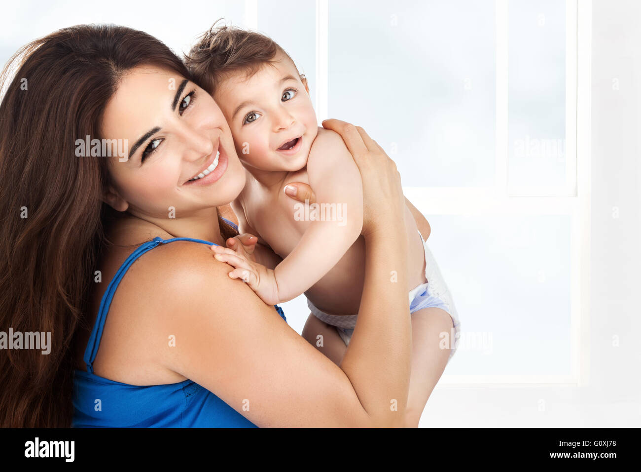 Cheerful young mother with her cute little son playing at home, with pleasure spending time ...