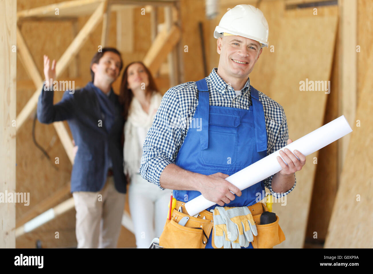 Worker holding house design plans and a young couple at construction ...