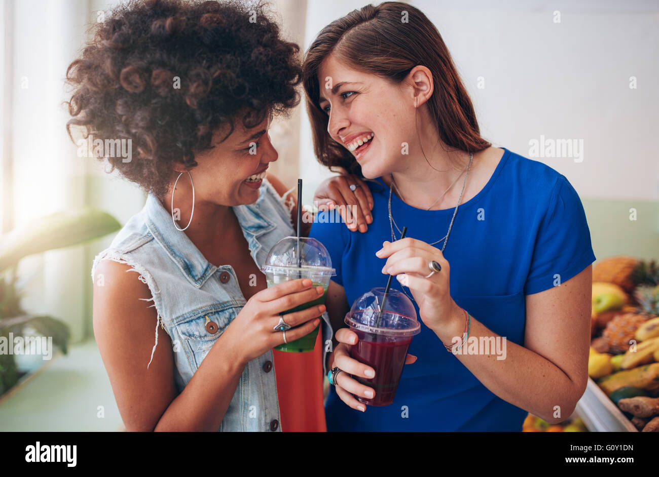 Portrait of cheerful young friends having fresh juice. Two young women ...