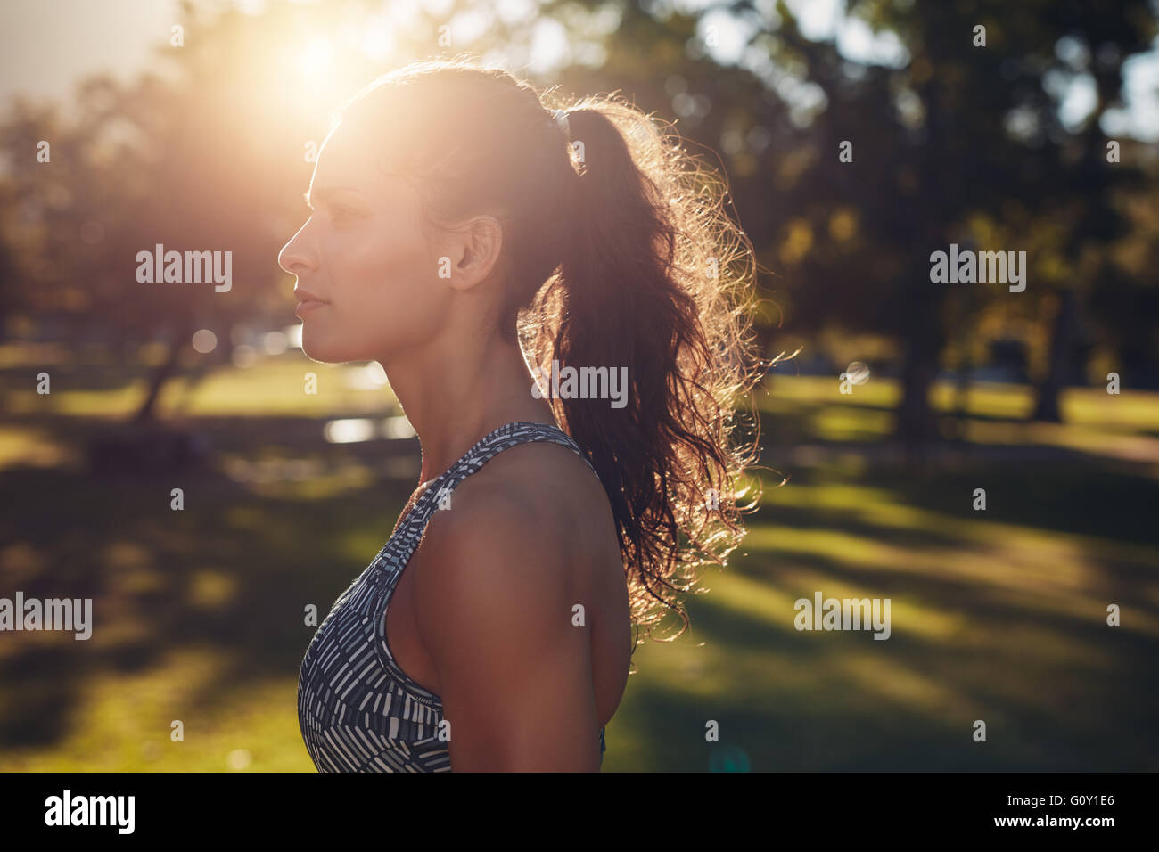 Side view shot of fit young woman in sports bra standing at the park on ...