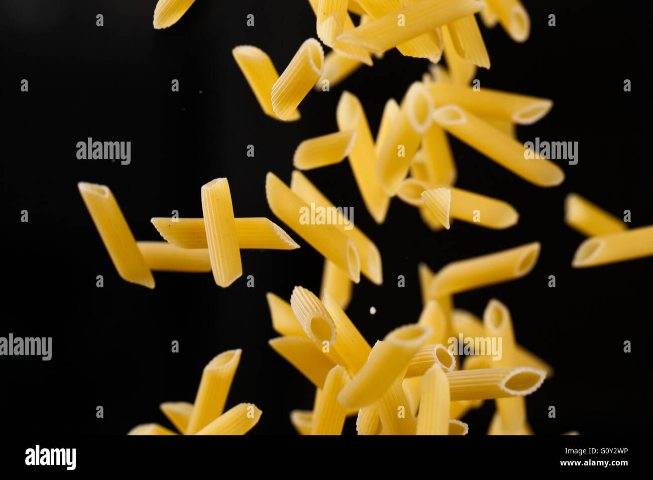 Falling penne pasta. Flying yellow raw macaroni over black background ...
