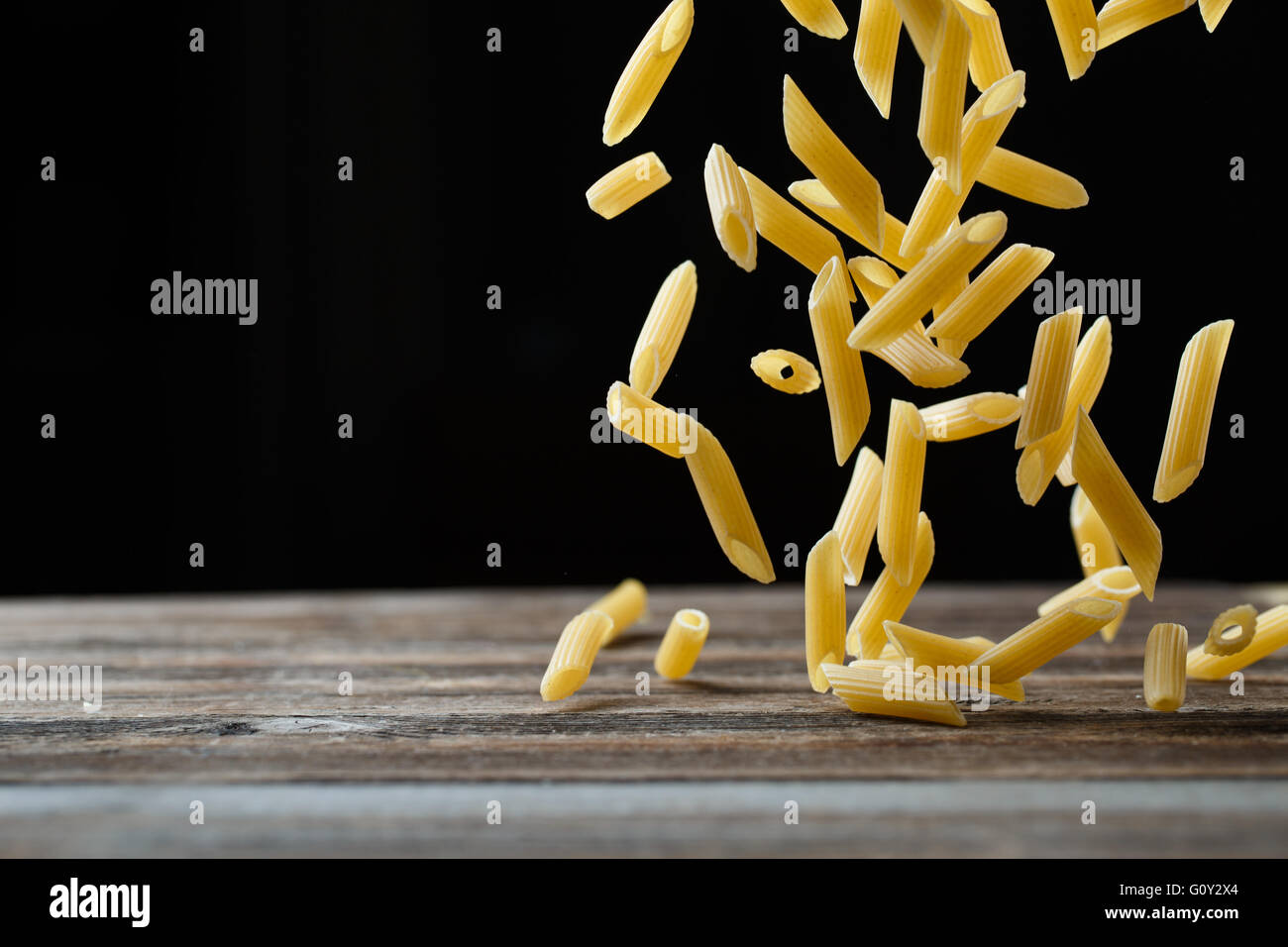 Falling penne pasta. Flying yellow raw macaroni over black background ...