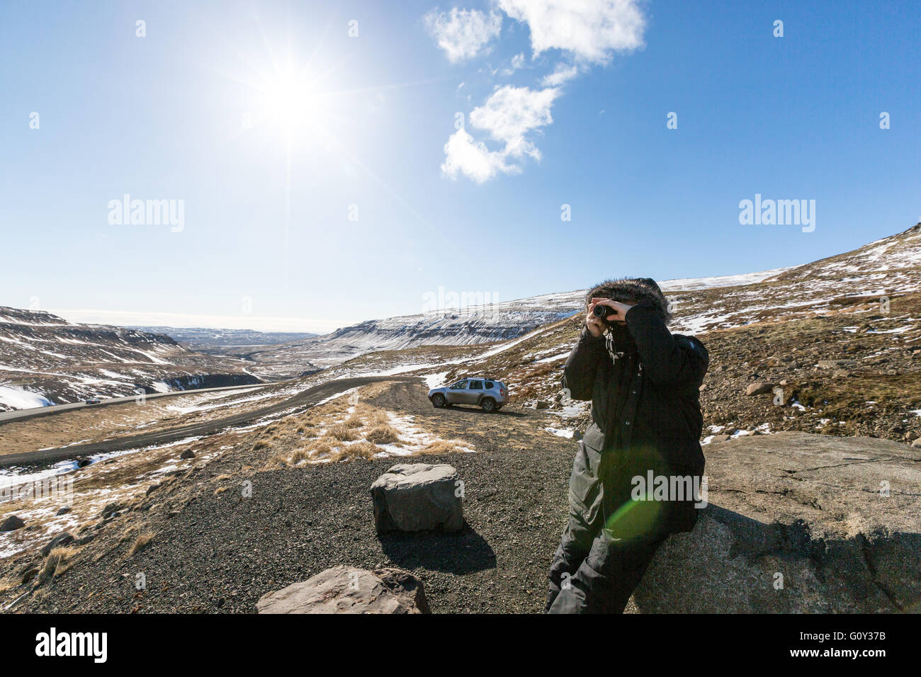 A tourist in full winter gear taking a photo in an Icelandic landscape ...
