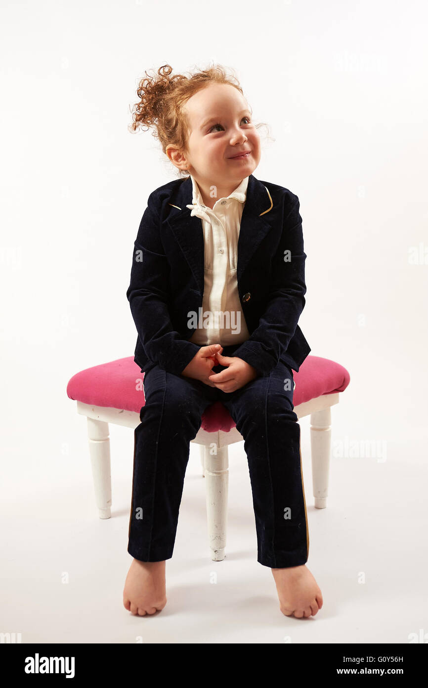 Little girl in black suit sitting on a rose stool and pouting Stock ...