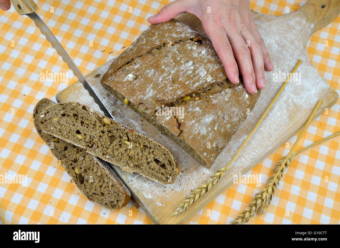 Someone is cutting dark rustic bread with knife Stock Photo - Alamy