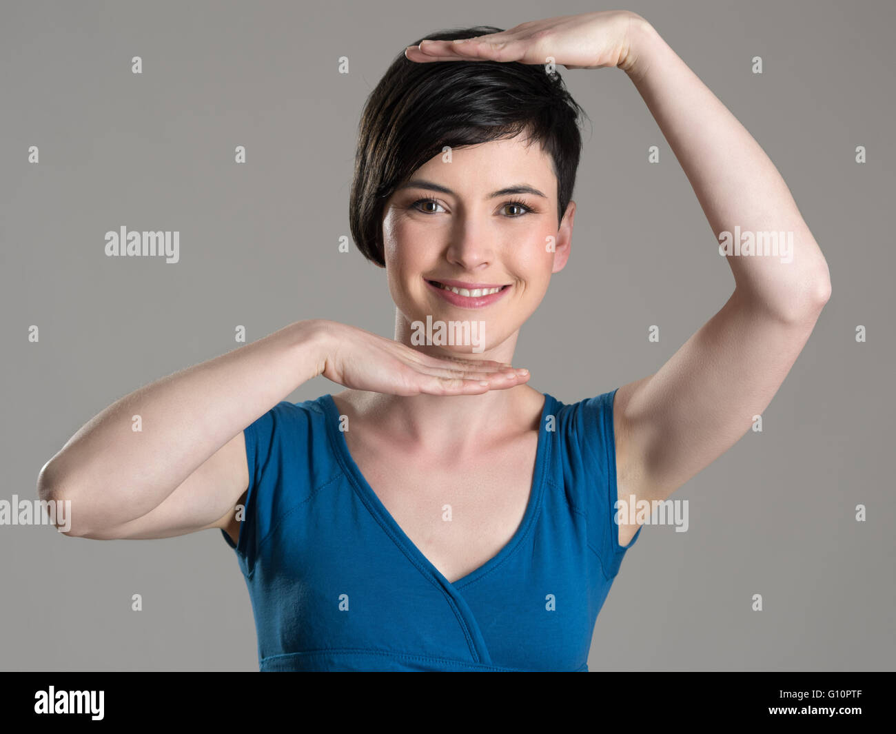 Studio portrait of young brunette cutie framing hands over gray ...