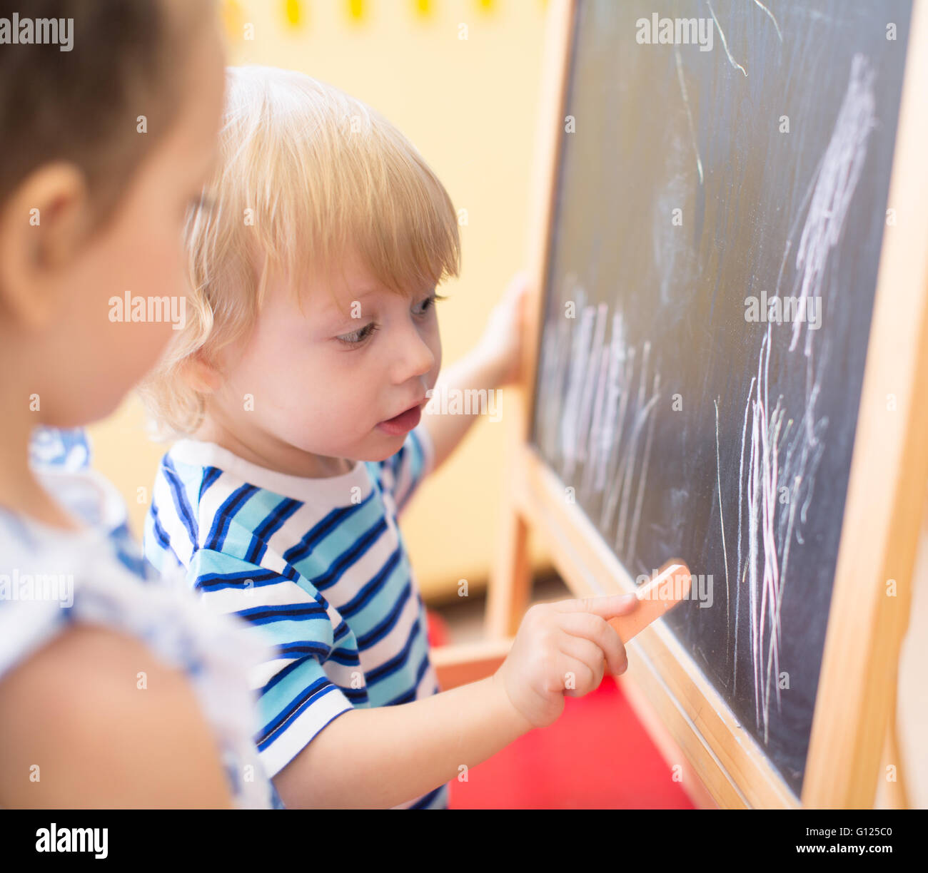 Little kids with chalk near blackboard side view Stock Photo - Alamy