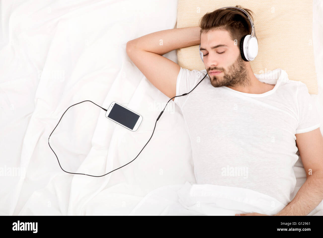 Portrait of a man from above with headphones and smartphone in bed ...
