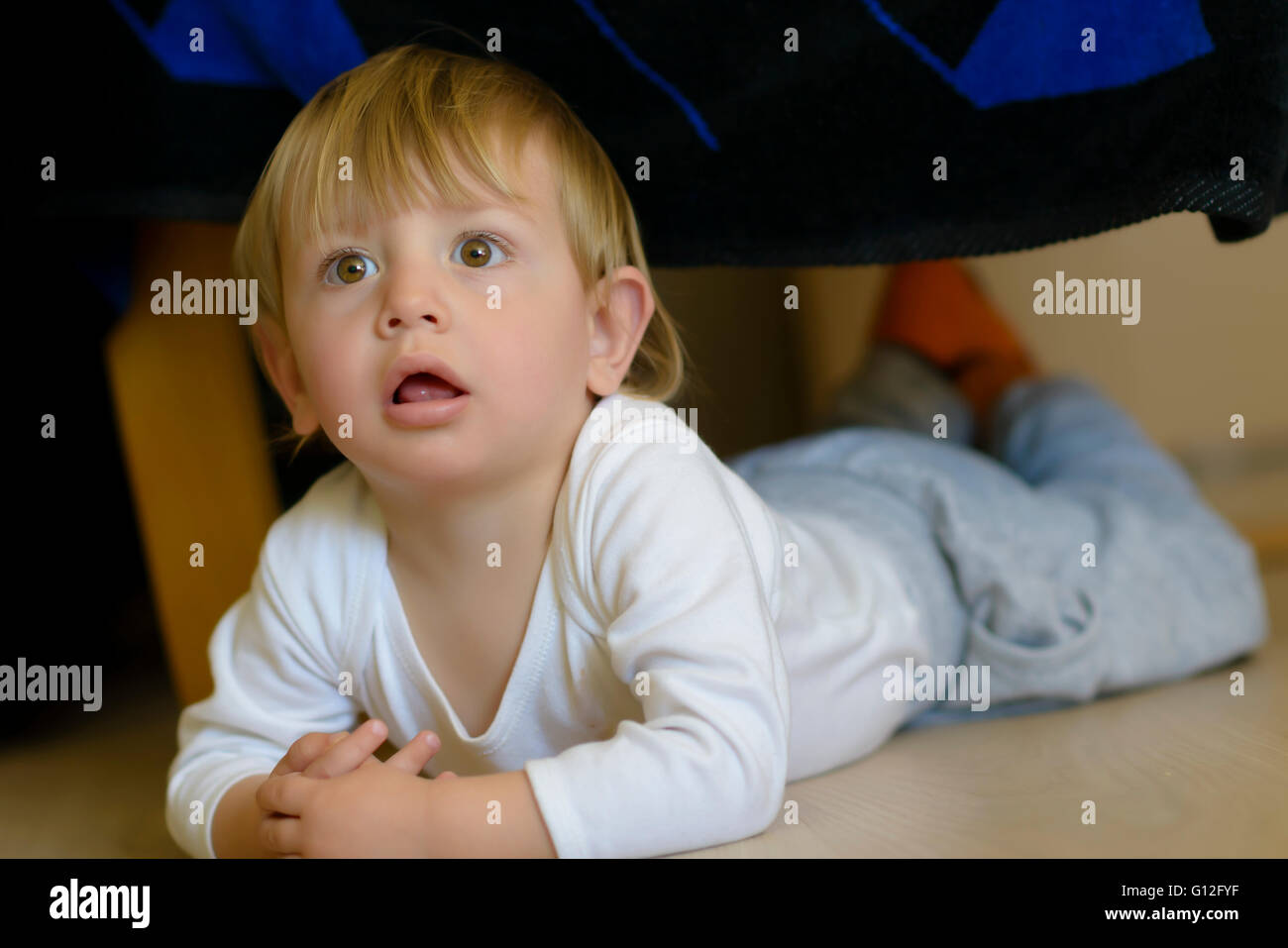 Cute baby looking curious under chair Stock Photo - Alamy