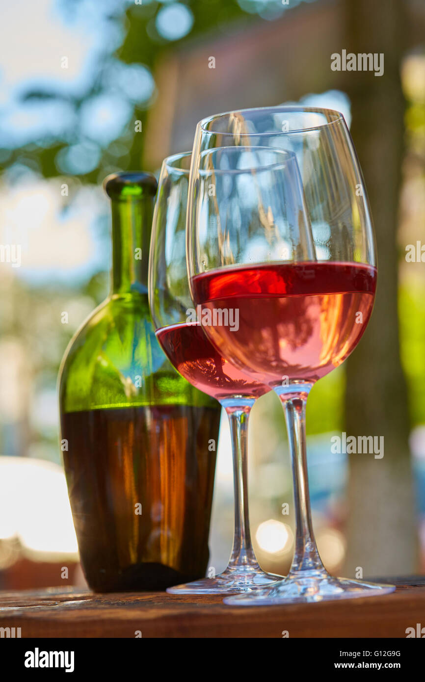 two wine glasses filled with red wine and wine bottle in background ...