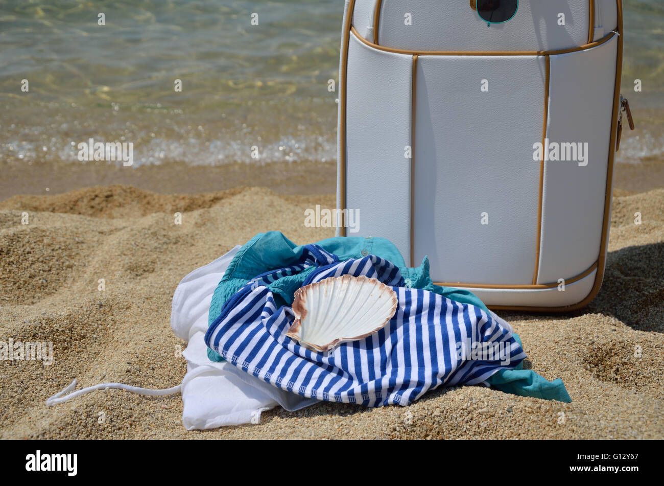 Suitcase and clothes on sandy beach with sea in background Stock Photo ...
