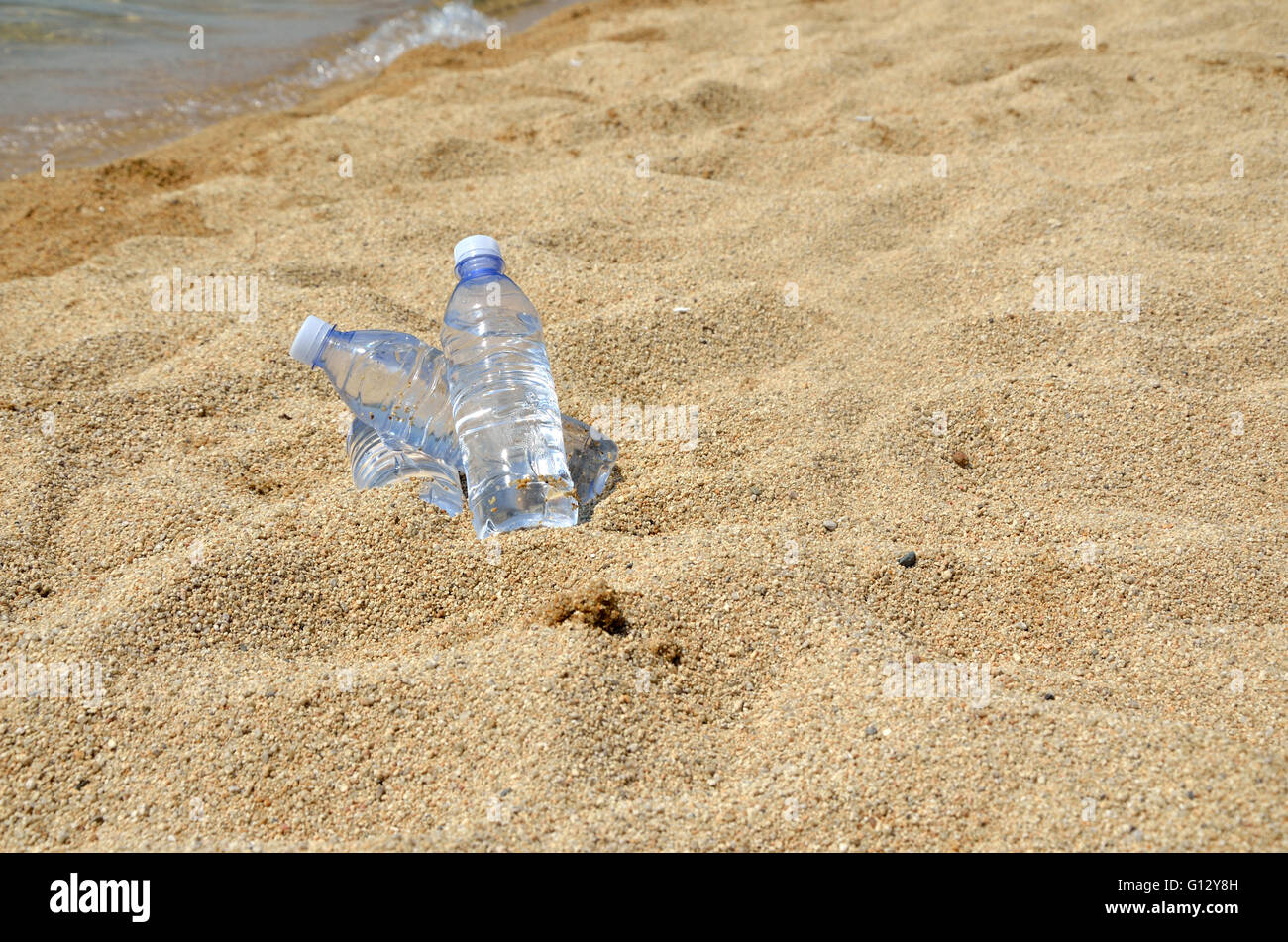Cold drinking water in transparent bottles on sandy beach by the sea ...