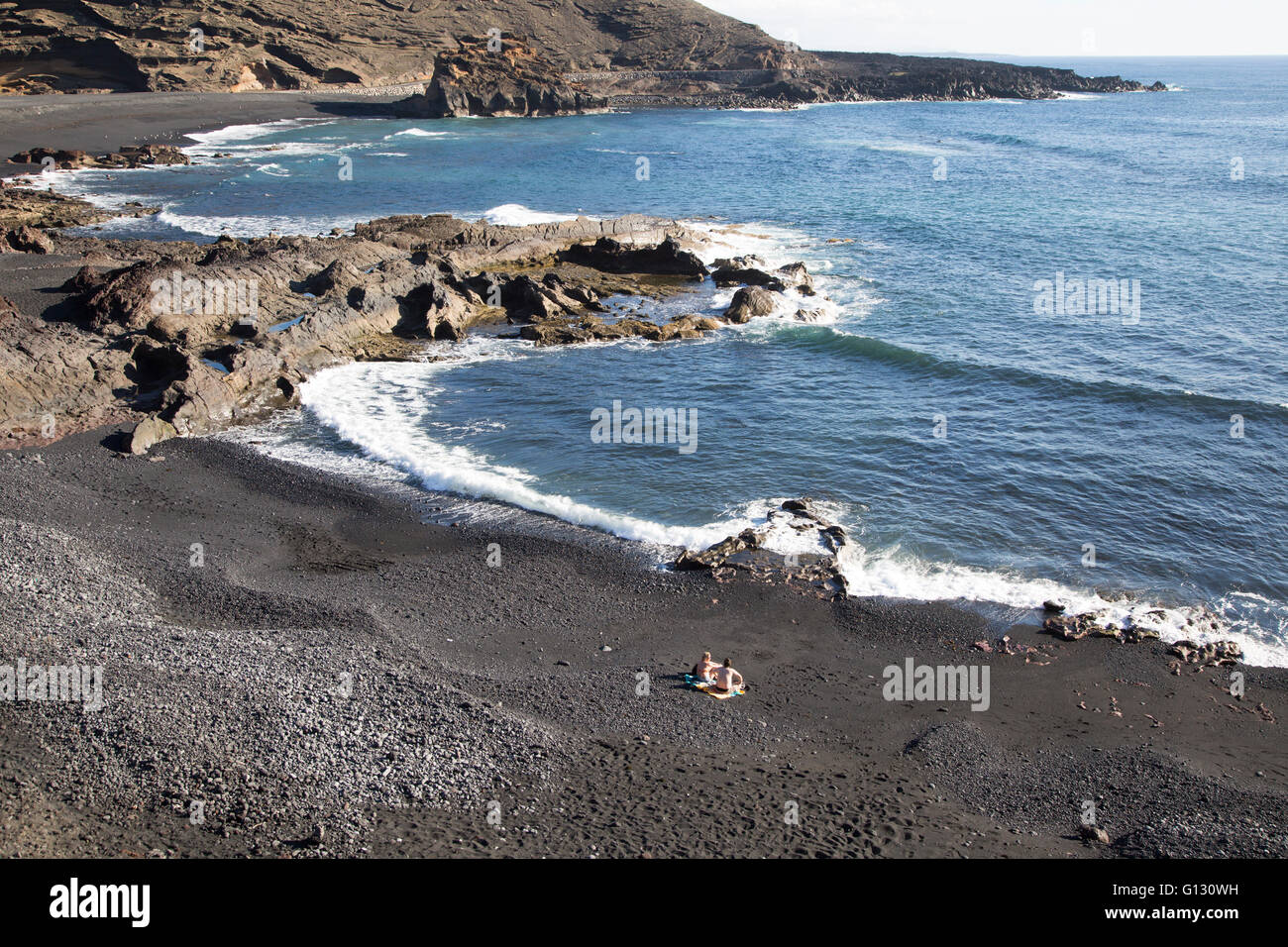 Two people sitting on black sand beach, El Golfo, Lanzarote, Canary ...