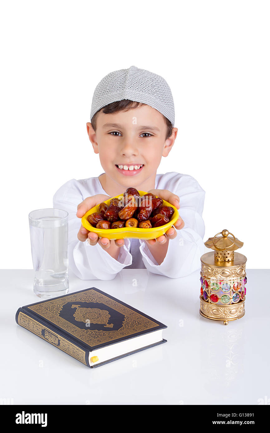 Little Muslim kid smiling while presenting a dish of dates for iftar ...