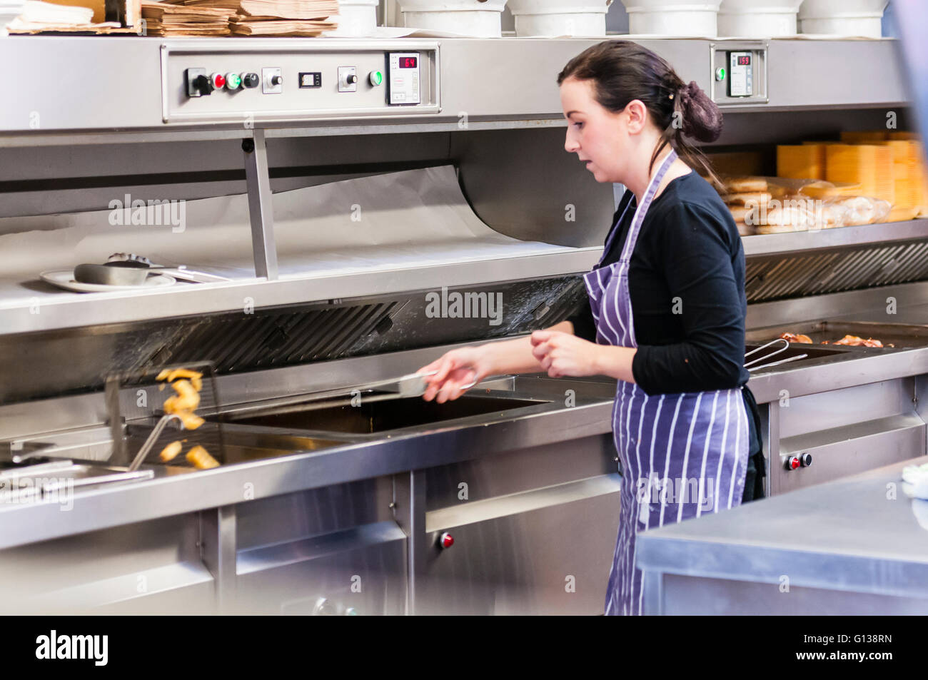 A woman tips cooked chips into a dispenser in a fish and chip shop ...