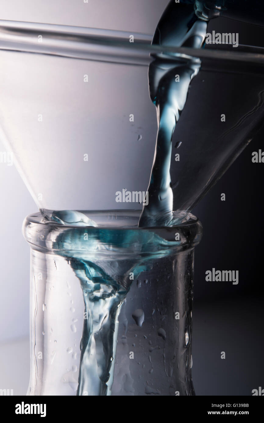 closeup of blue chemistry pouring through a funnel into Erlenmeyer ...