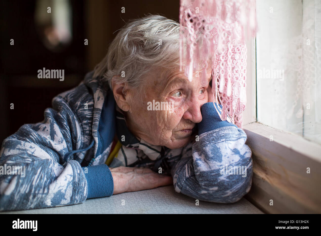 An elderly woman sadly looking out the window Stock Photo - Alamy