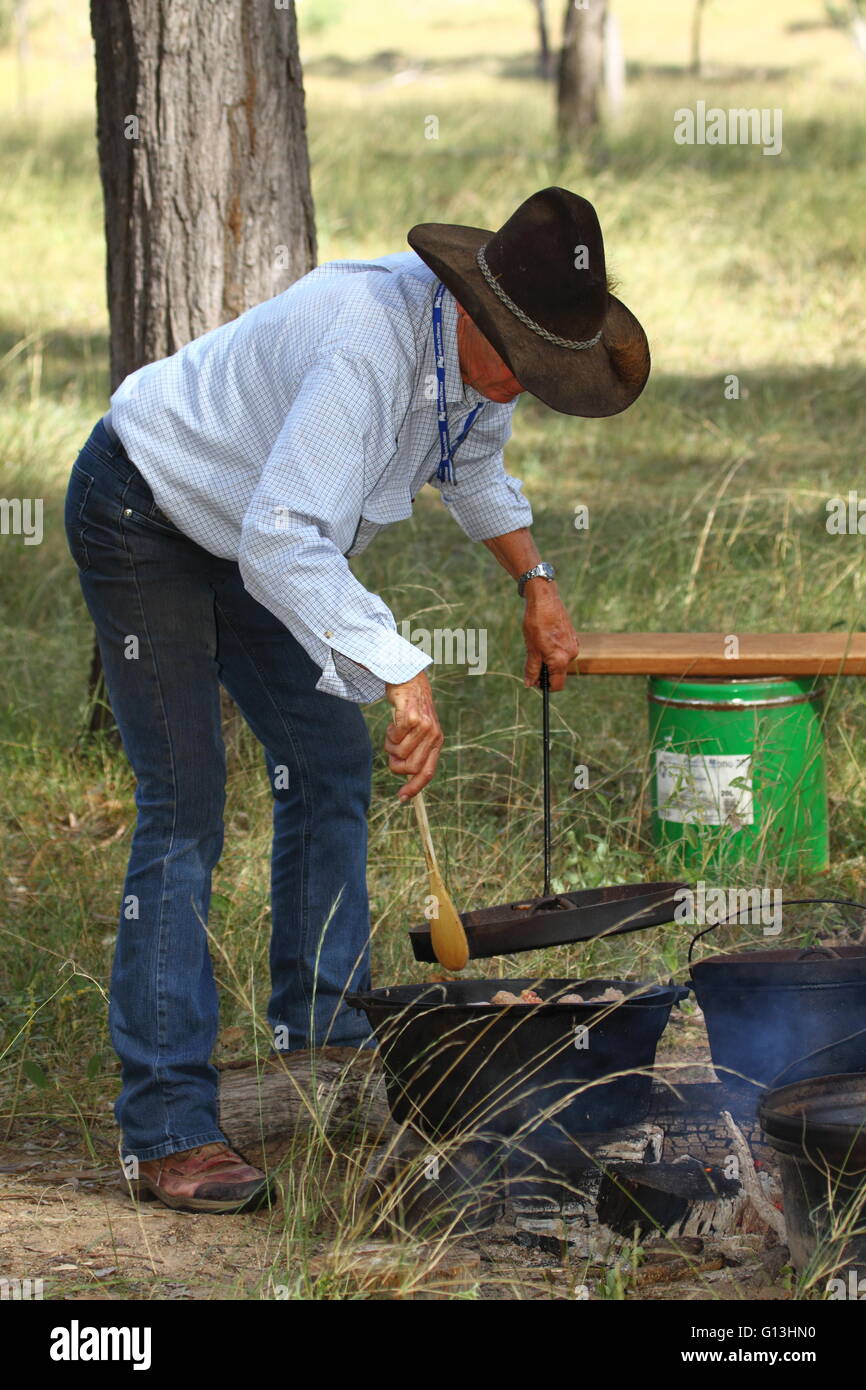 A mature country lady cooking with camp ovens, or dutch ovens, in a ...