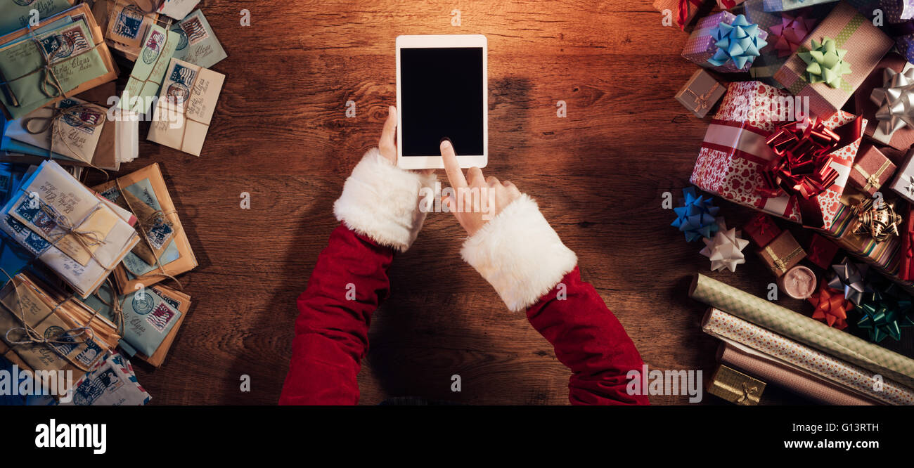 Santa Claus sitting at his desk and using a digital touch screen tablet ...