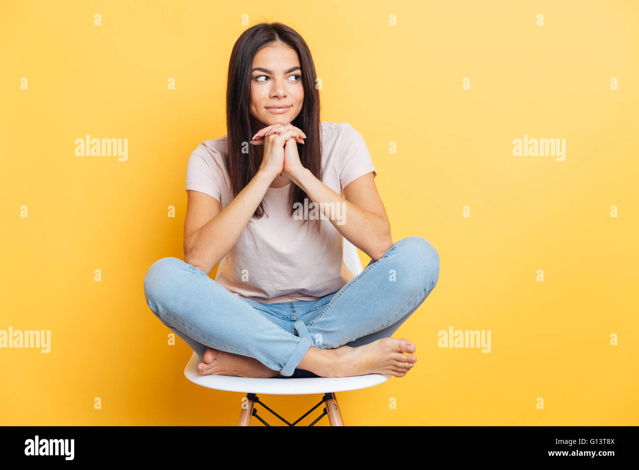 Happy cute woman sitting on the chair and looking away over yellow ...