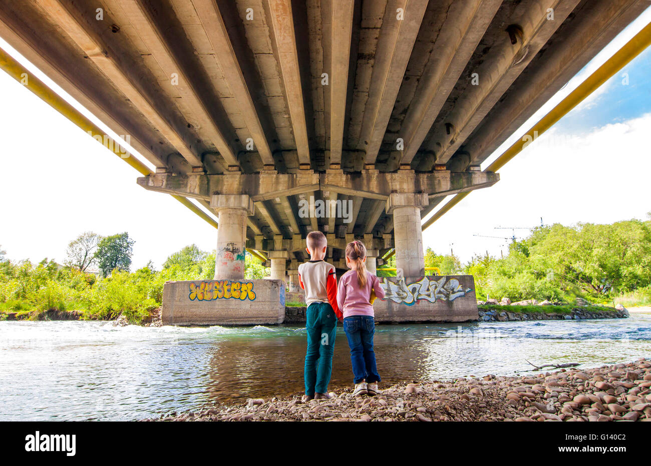 Boy and girl standing under the bridge near river Stock Photo - Alamy
