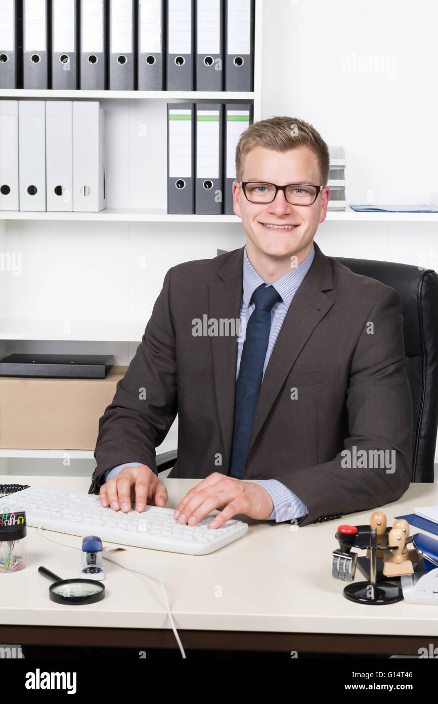 Young smiling businessman with glasses is typing at the computer ...