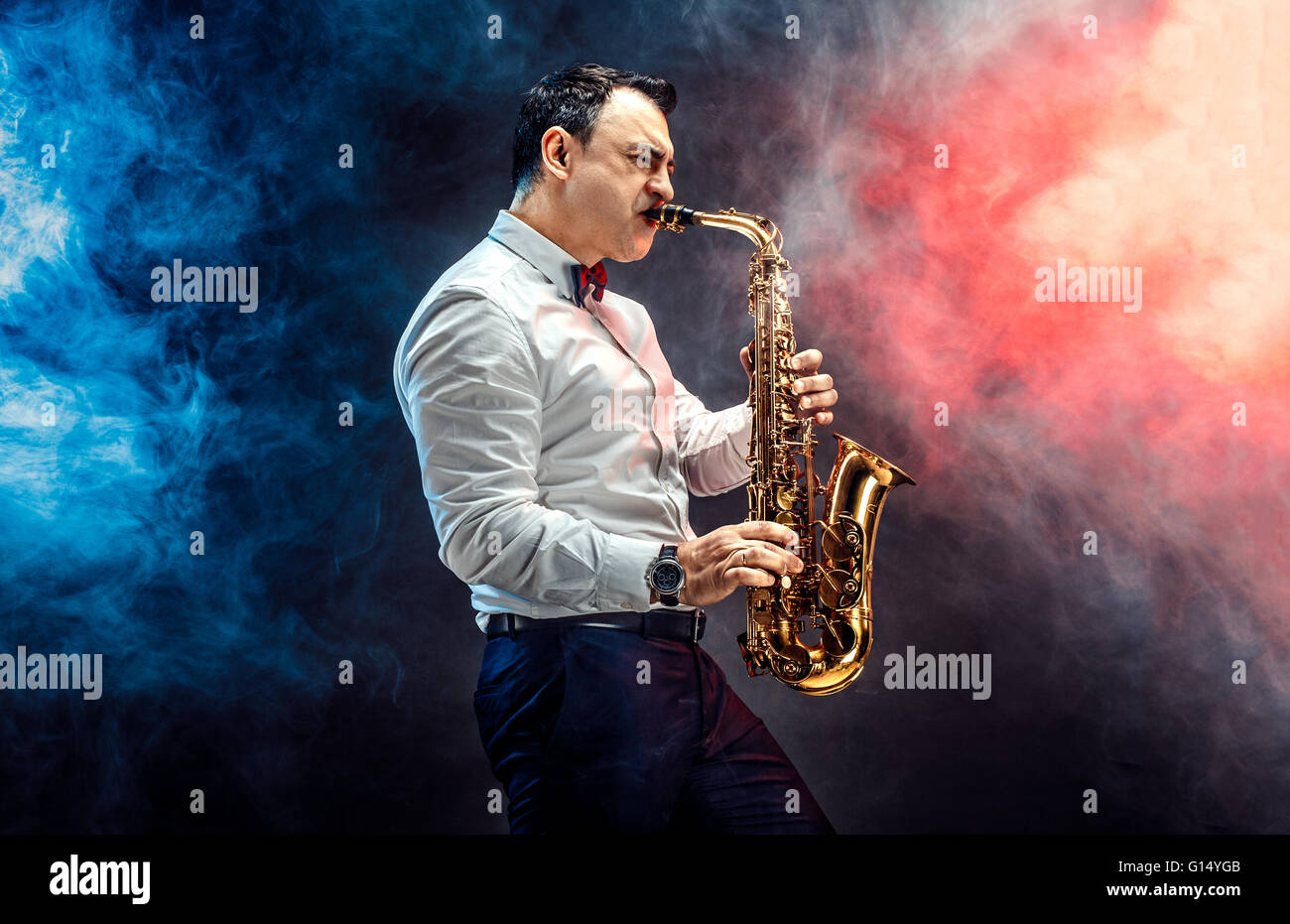 Side view of elegant handsome man playing saxophone in studio against ...