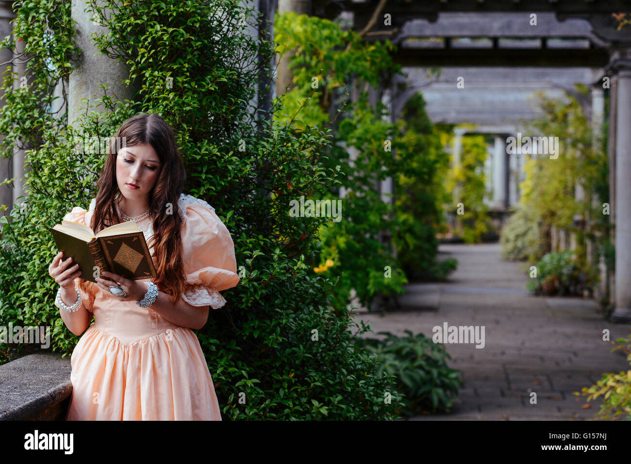 A young Victorian woman in pink dress is reading a book Stock Photo - Alamy