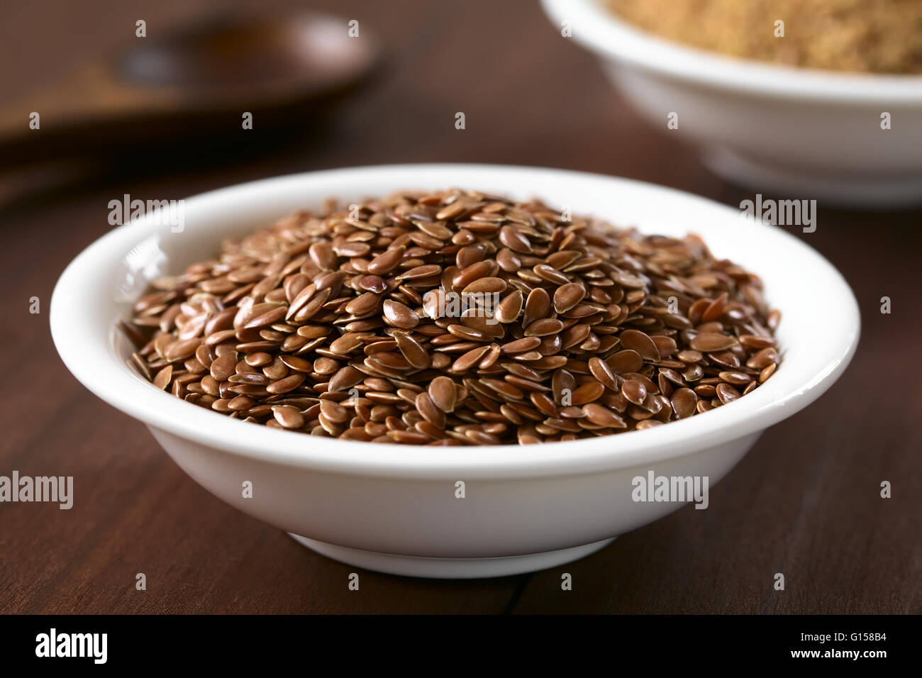 Brown flax seeds or linseeds in small bowl, photographed on dark wood with natural light ...
