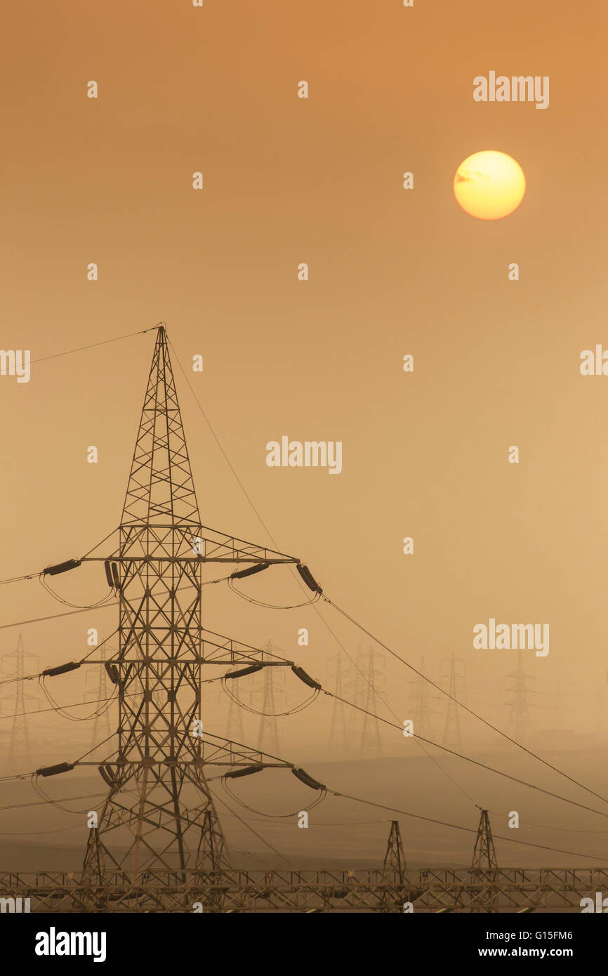 Power pylons stretch into the distance, sun rises through air thick ...