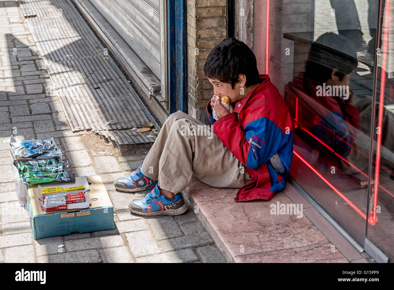 A young boy selling gum and candy on the sidewalk as he eats his lunch ...