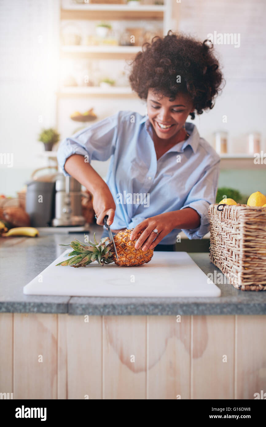 Young african woman standing behind bar counter cutting a pineapple on ...