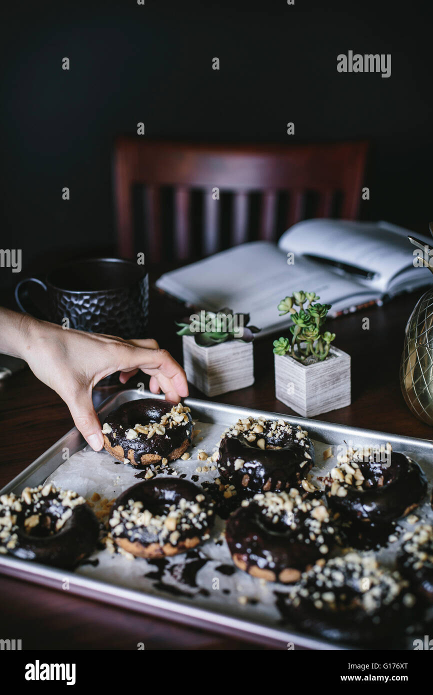 A woman is taking a donut from a tray full of chocolate glazed banana ...