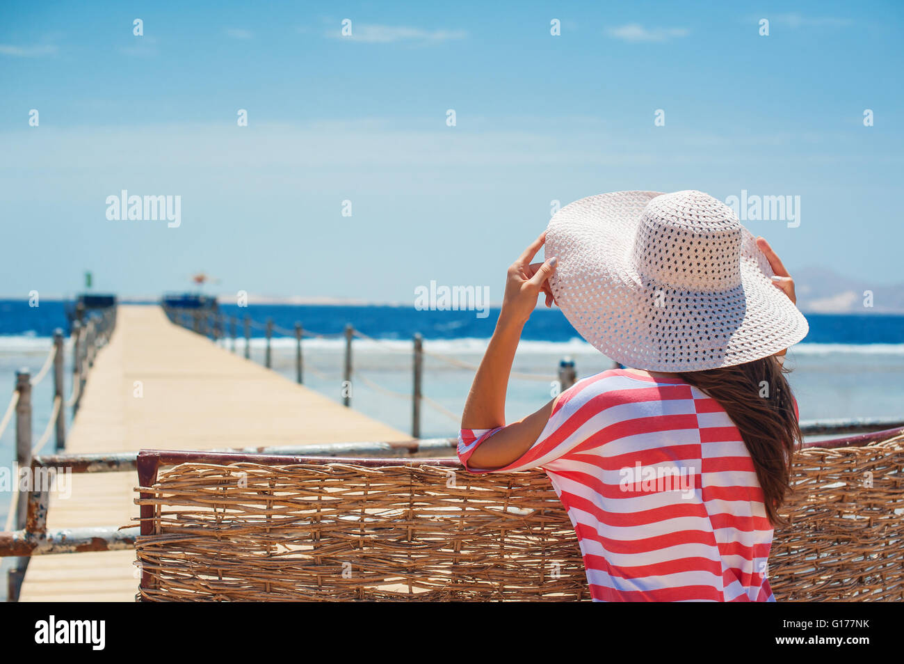 Closeup back view of woman in white hat looking out towards blue ocean ...