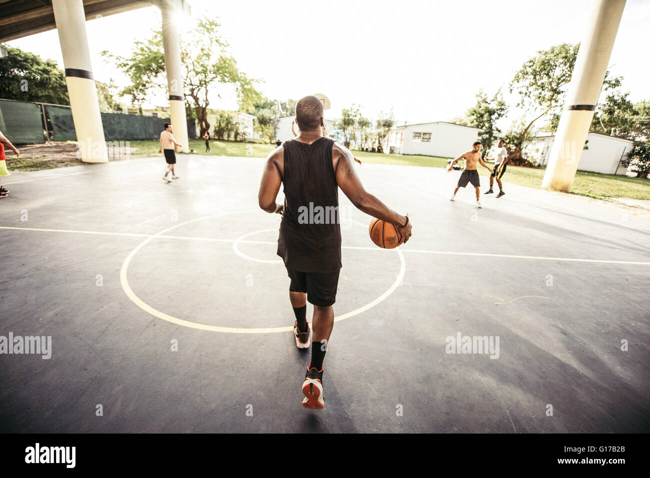 Full length rear view of young man walking on basketball court holding ...