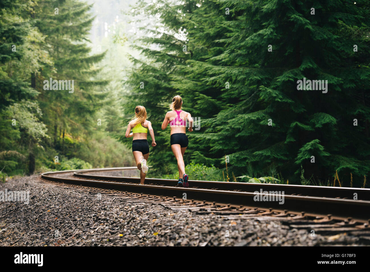 Young woman and teenage girl running along rural train track, rear view ...