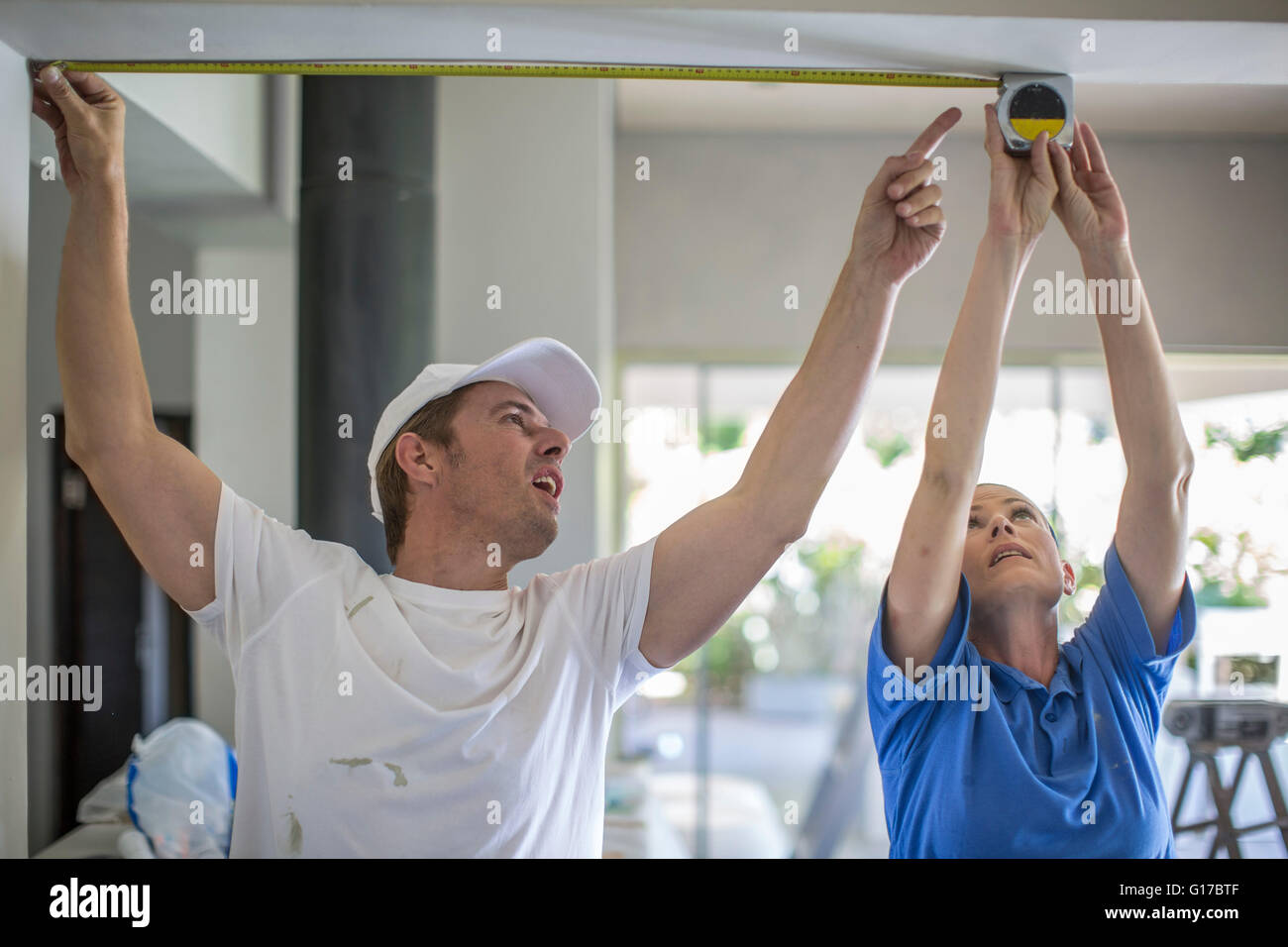 Couple, arms raised, using tape measure to measure ceiling Stock Photo ...
