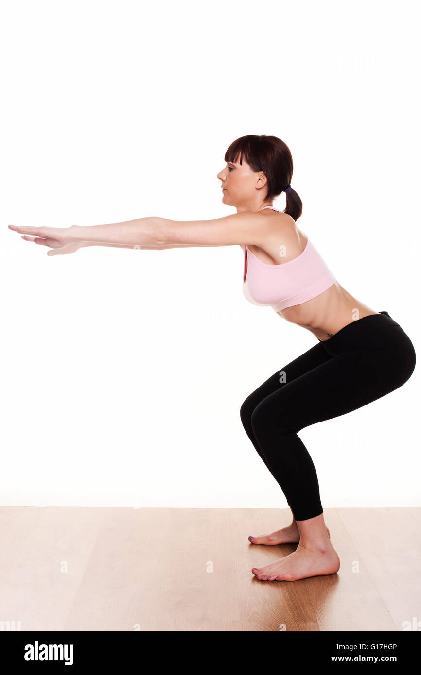 Woman wearing pink tank top and black exercise pants, doing a squat ...