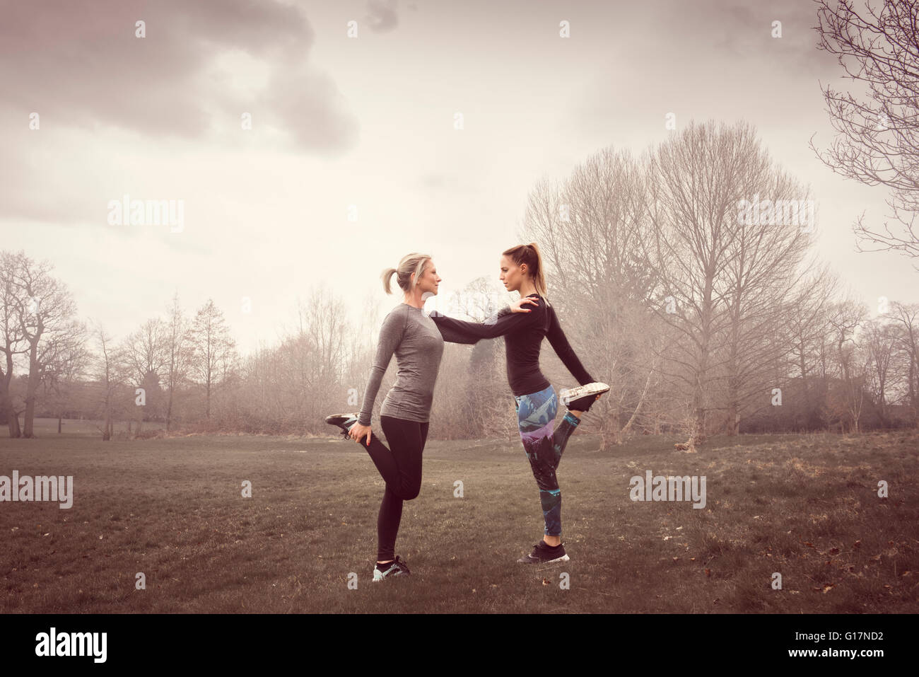 Full length side view of women face to face on one leg, hands on each ...