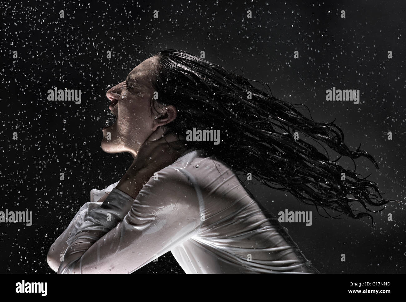 Side view of woman wearing white shirt drenched in rain throwing back ...