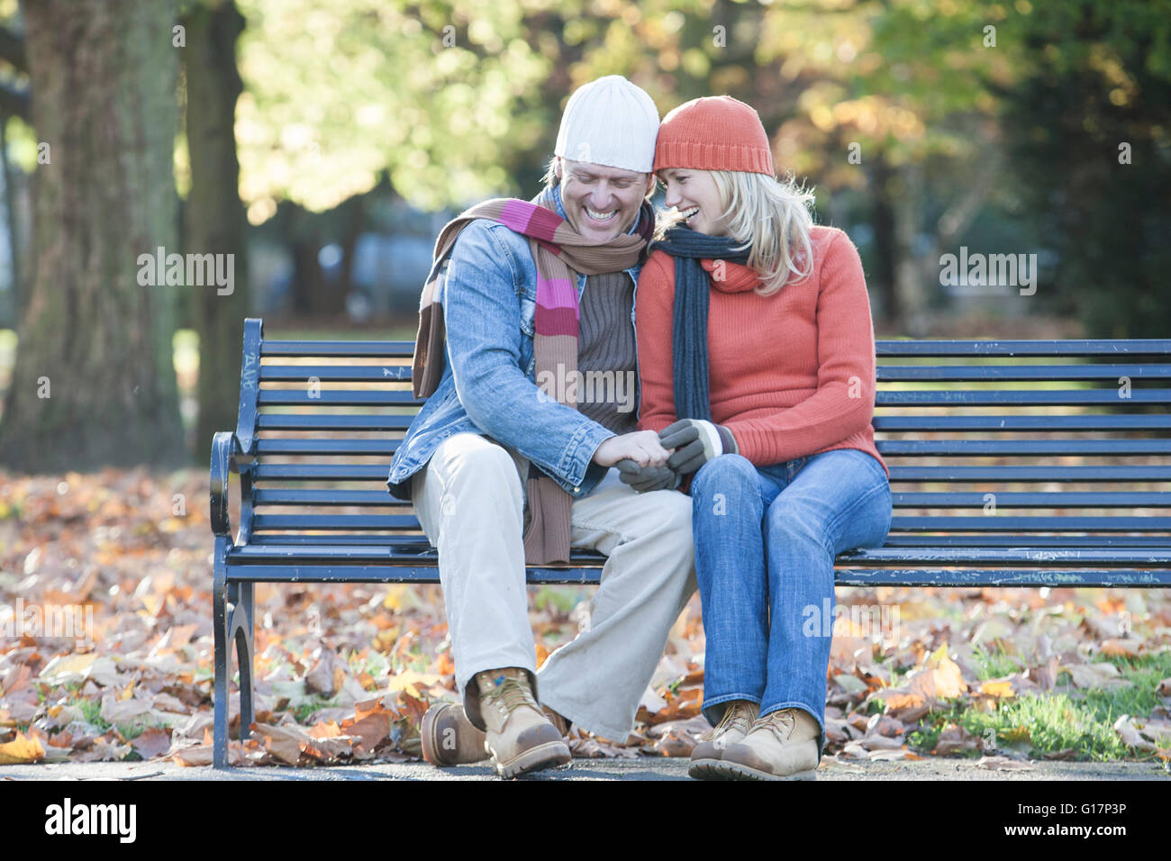 Heterosexual couple sitting together on park bench, holding hands ...