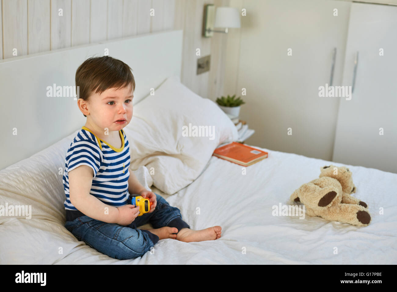 Sad baby boy sitting on bed holding toy car, looking away Stock Photo ...