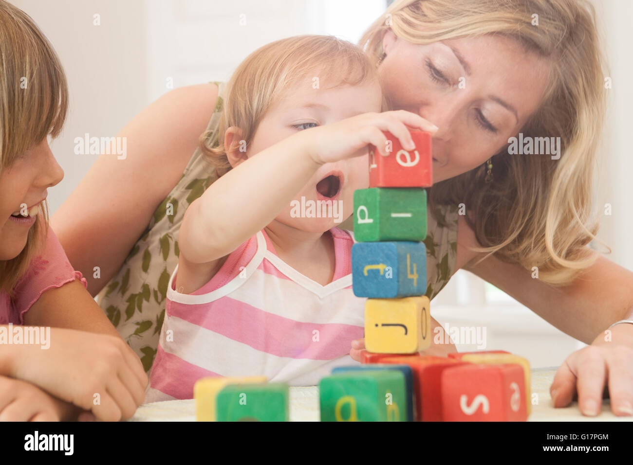 Mother and big sister watching baby girl stack building blocks Stock ...