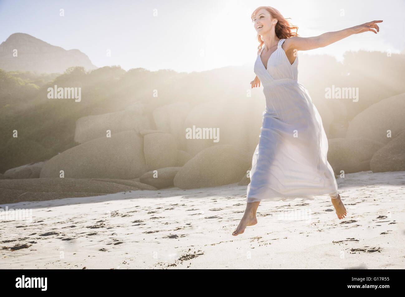 Woman wearing white dress, arms open jumping on beach Stock Photo - Alamy